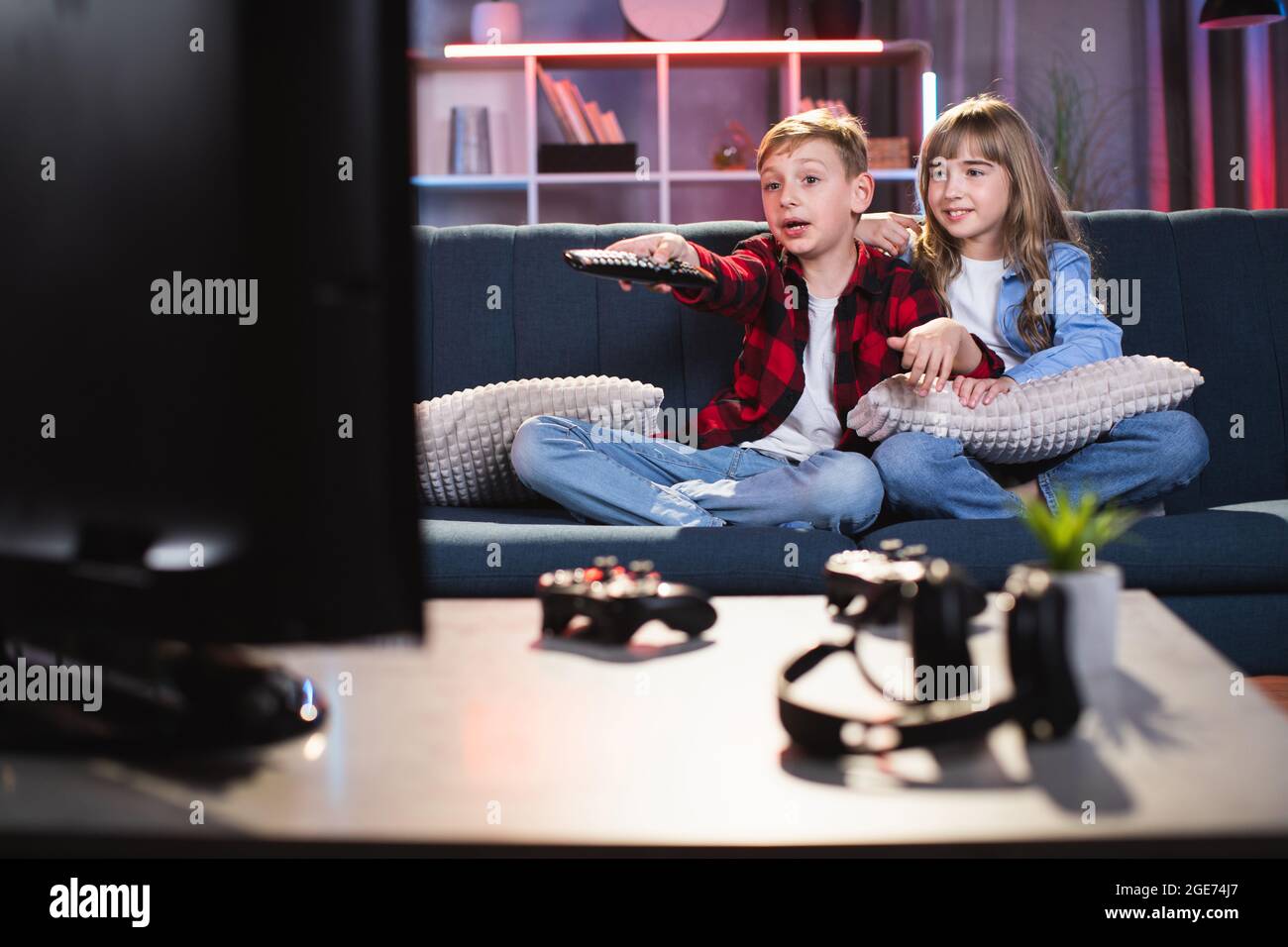 Happy caucasian kids using remote control for choosing cartoon on TV ...