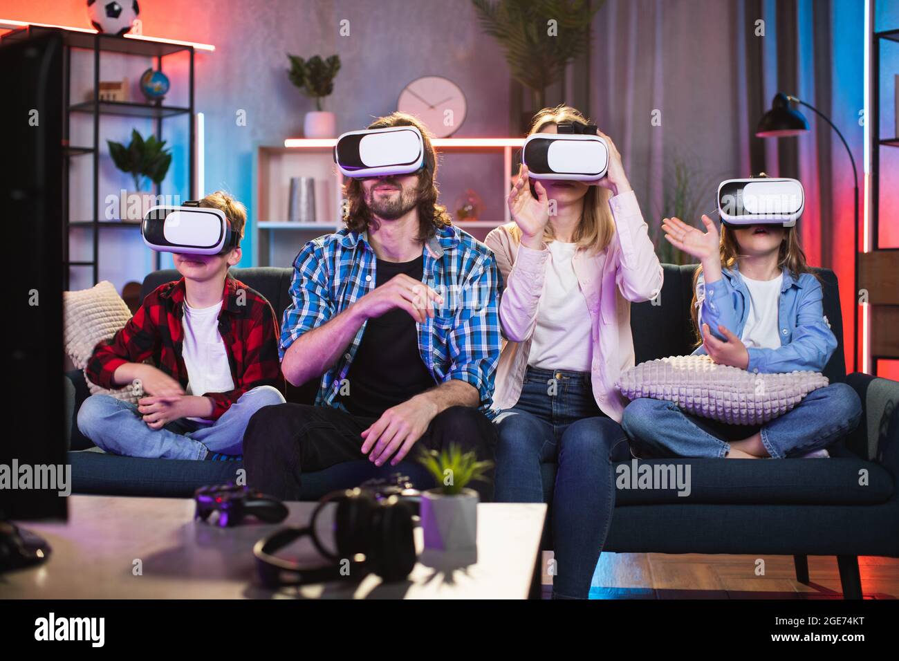 Happy young parents with two kids sitting on cozy sofa and wearing VR ...
