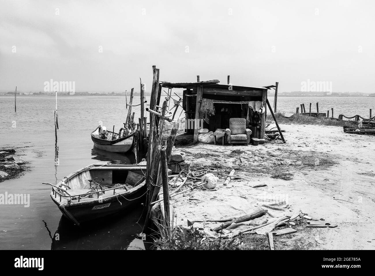 Grayscale shot of a dock with small wooden boats parked near it next to ...