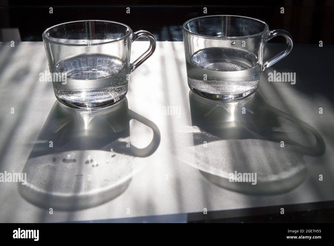 Two clear glass cups with water and their shadows on a table Stock ...