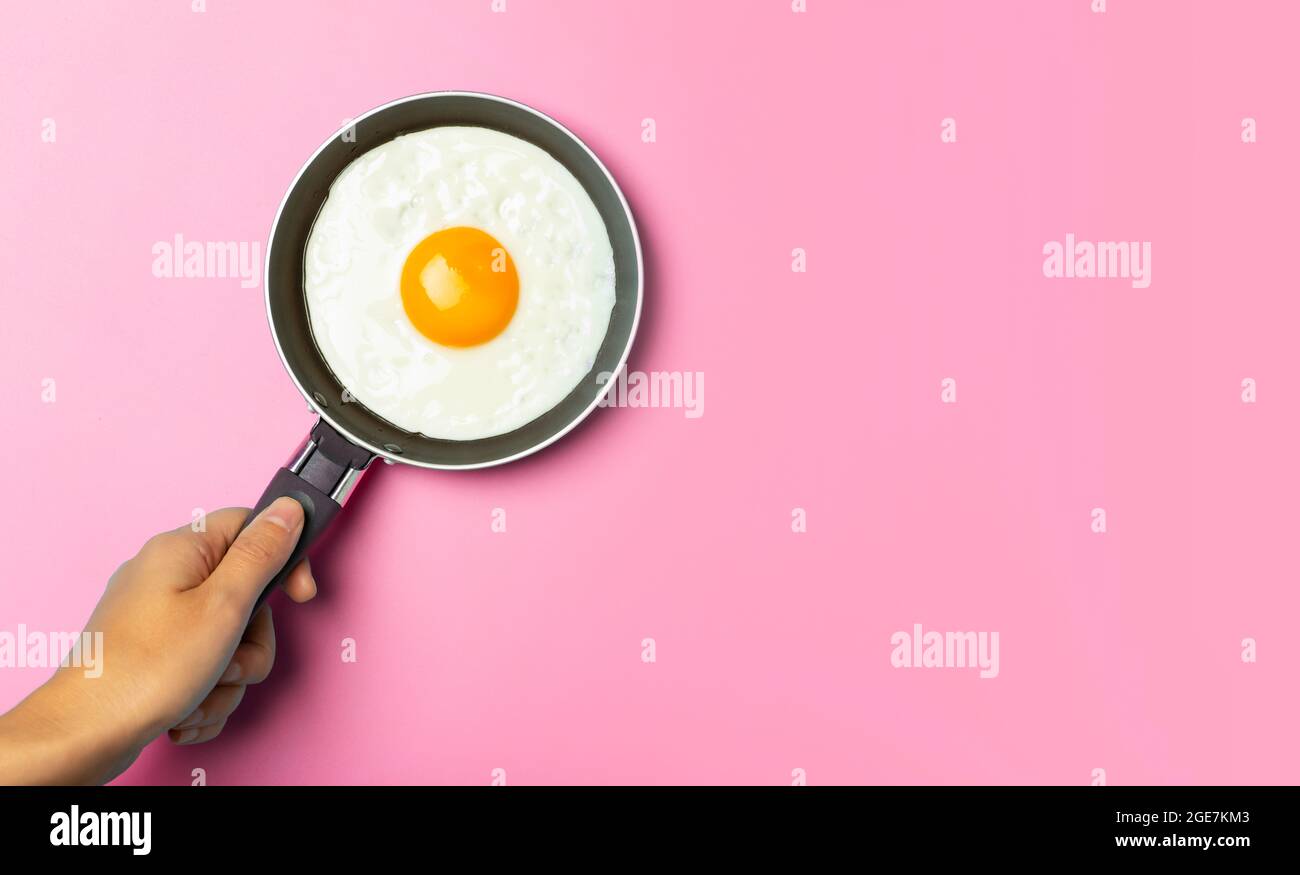 Fried egg is minimal. Fried egg in a frying pan on an empty pink background. Creative breakfast ...