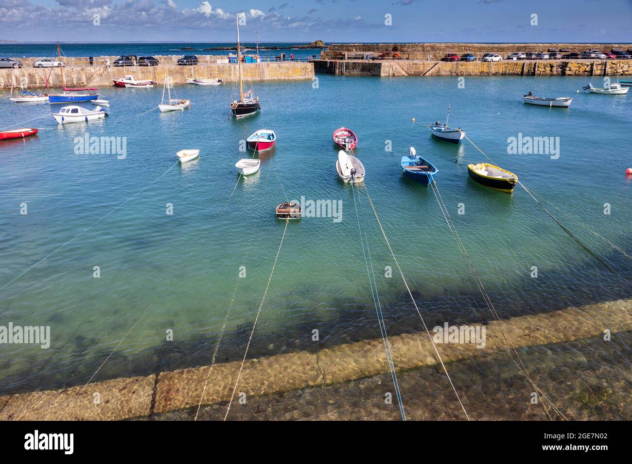 Mooring ropes lead out to tethered boats on the blue water of Mousehole ...