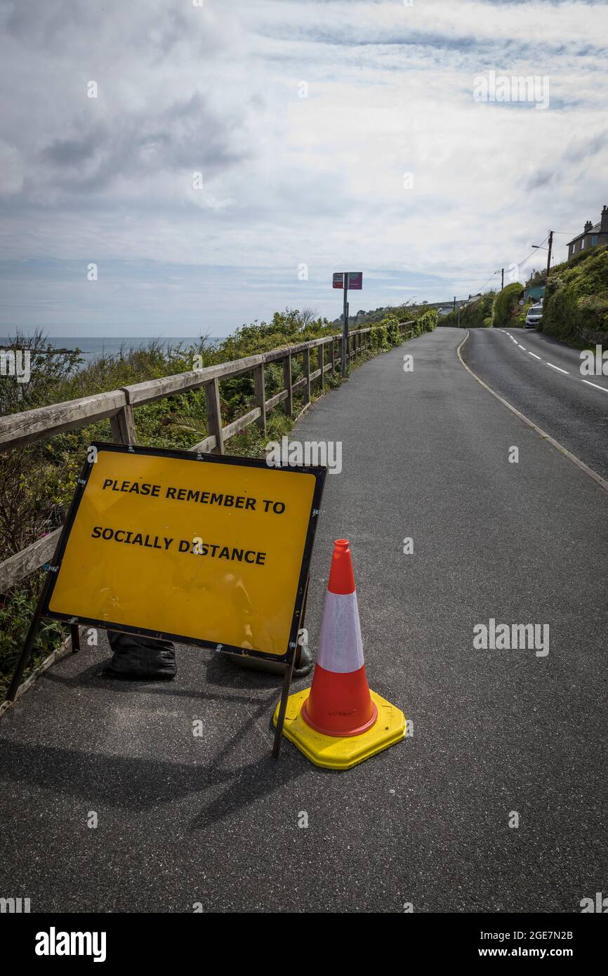 Roadside warning sign and cone reminding pedestrians to 'socially ...
