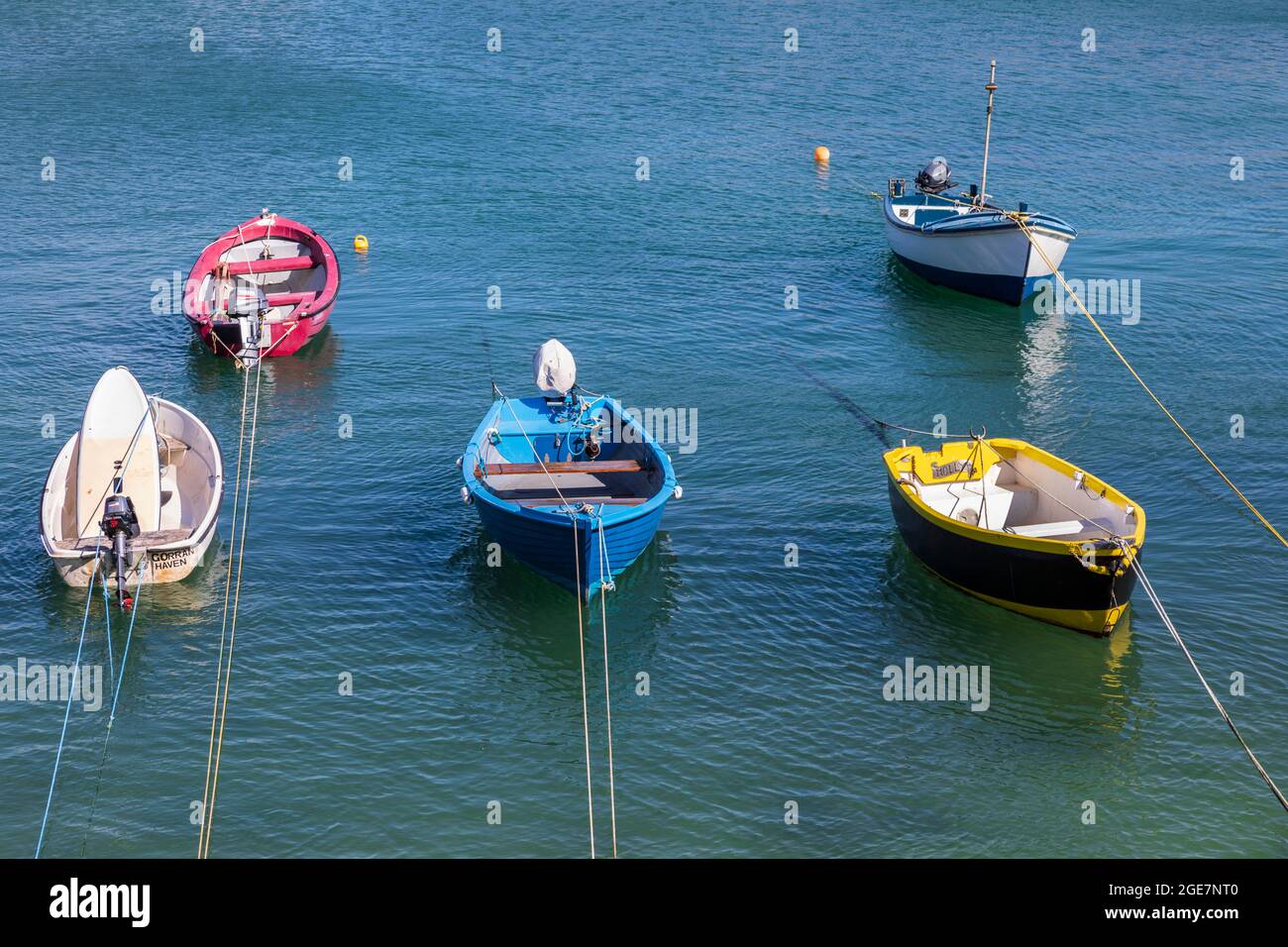 Mooring ropes lead out to tethered boats on the blue water of Mousehole ...