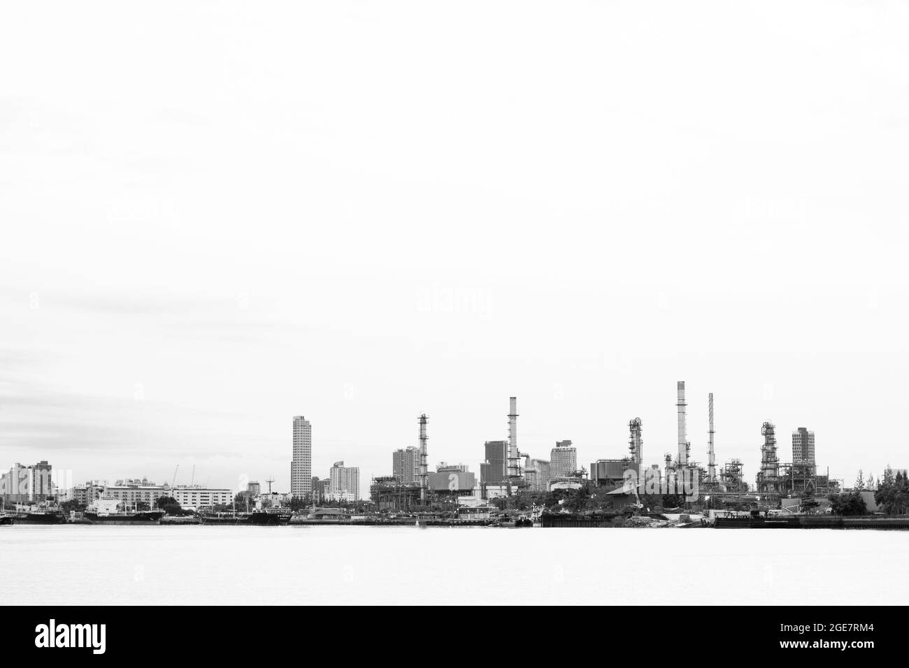 Grayscale view of factory with pipes against the lake under the cloudy ...