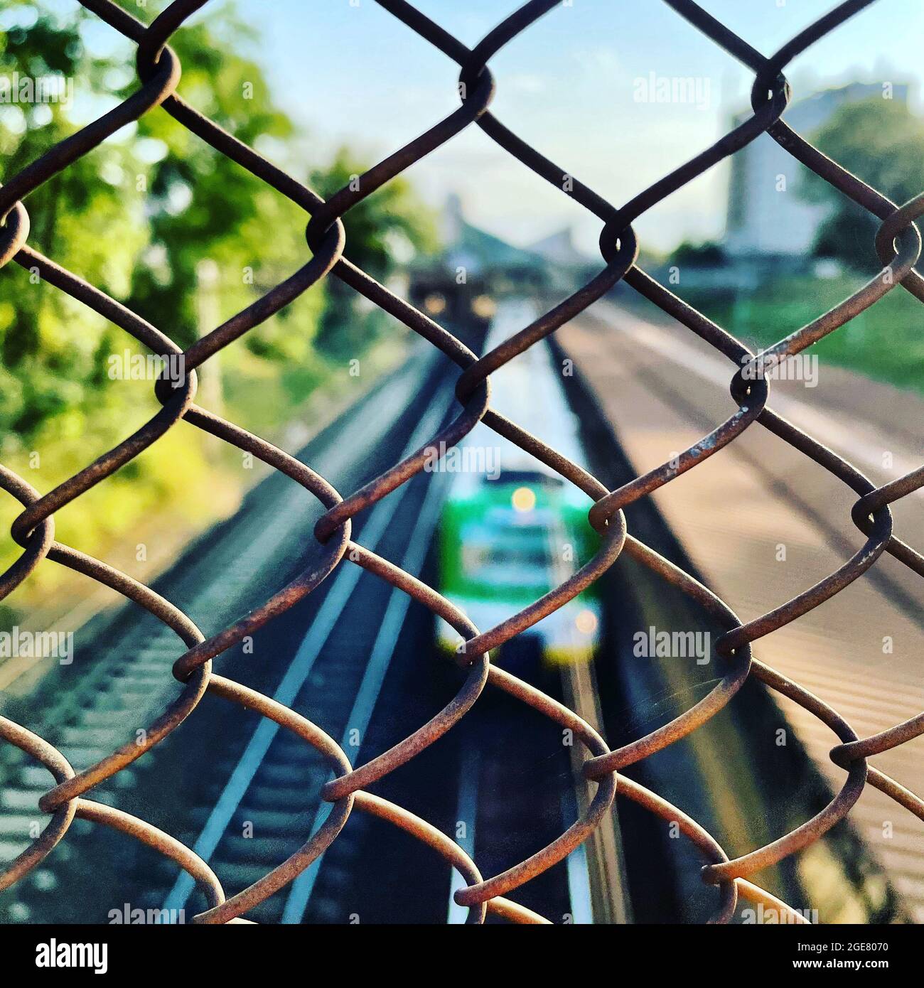 Train at a stop visible through a fence Stock Photo - Alamy