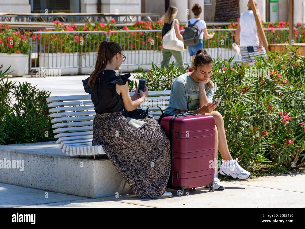SPLIT, CROATIA - Jun 04, 2021: Two girls with travel suitcase sitting ...