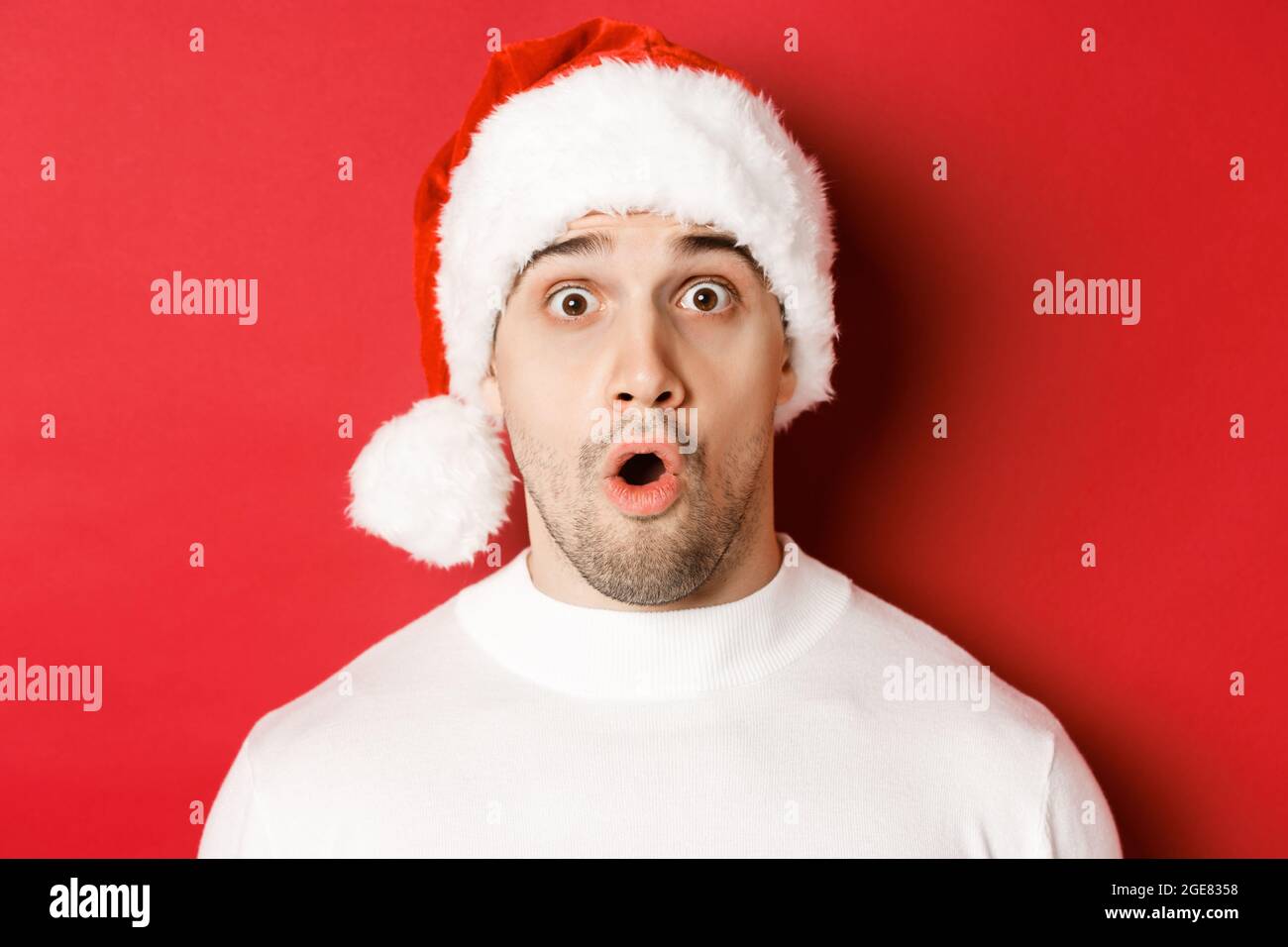 Close-up of attractive surprised man in santa hat, saying wow and ...