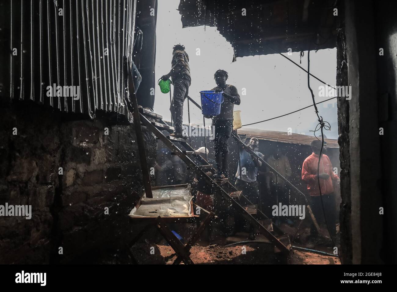 Locals climb to the roof with buckets of water to help put out a fire ...