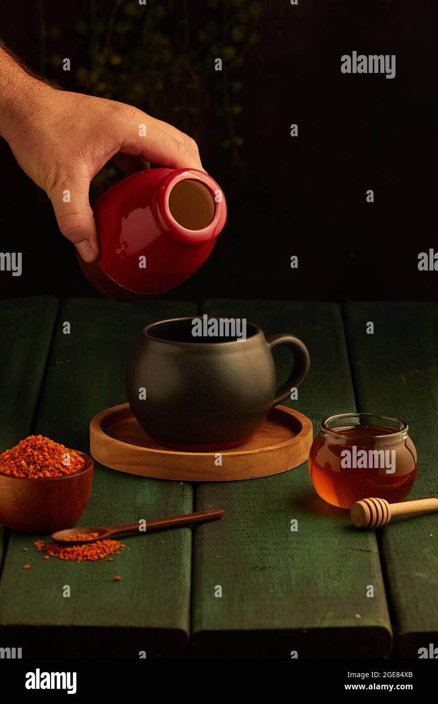 Vertical shot of a hand pouring something into a mug with a honey jar ...