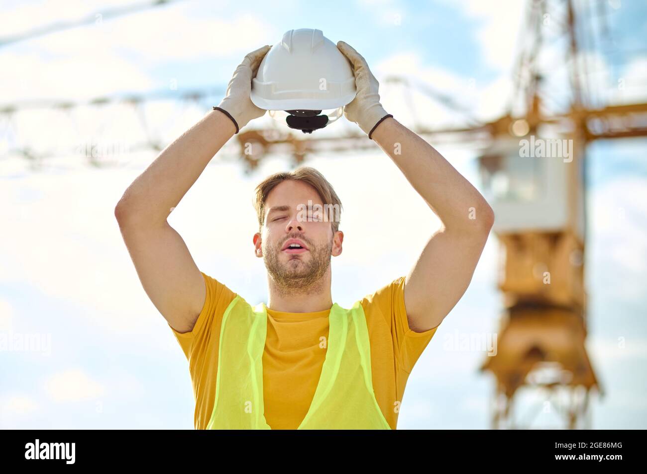 Exhausted worker with his eyes closed holding his hardhat overhead ...