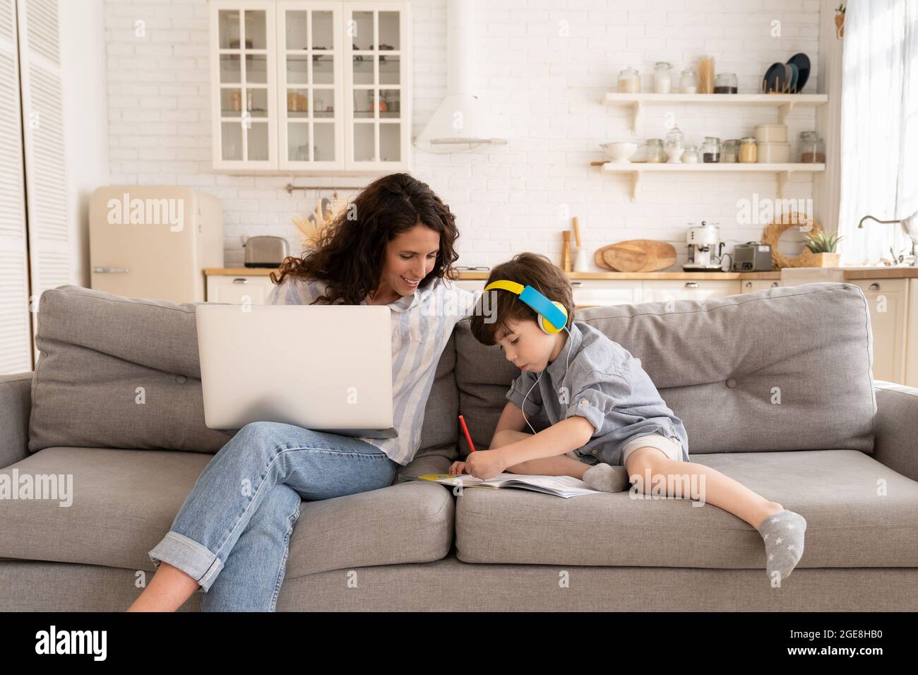 Loving mother look at son in headphones draw, using laptop and surfing ...