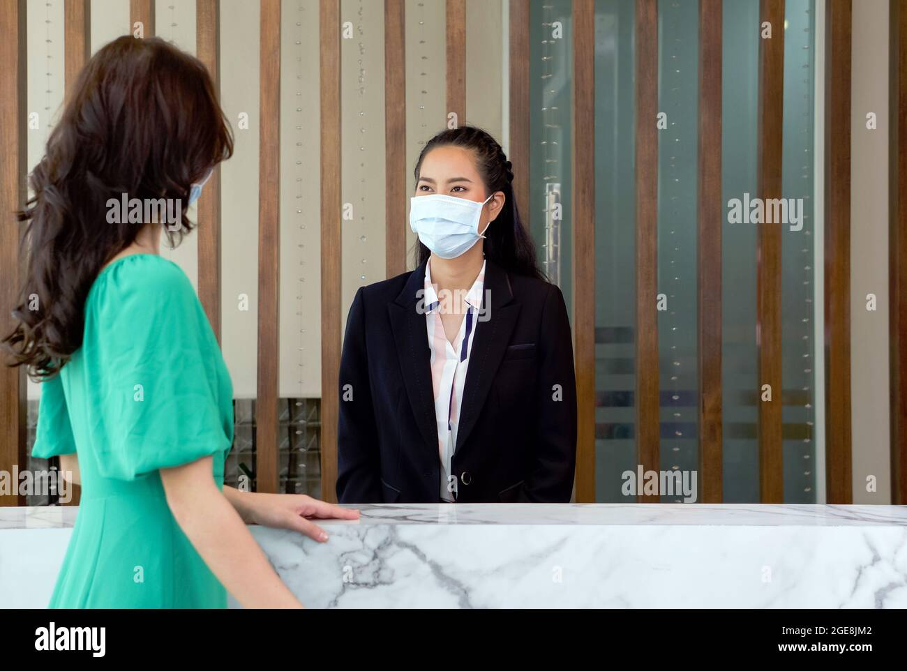 Hotel manager in black suit greets young caucasian tourist in green ...