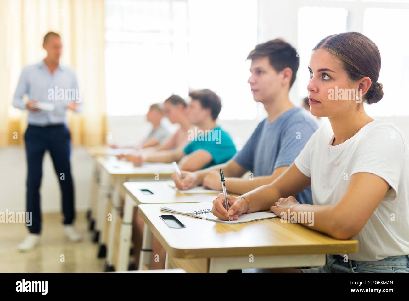Girl high school student listening to teacher and making notes during ...