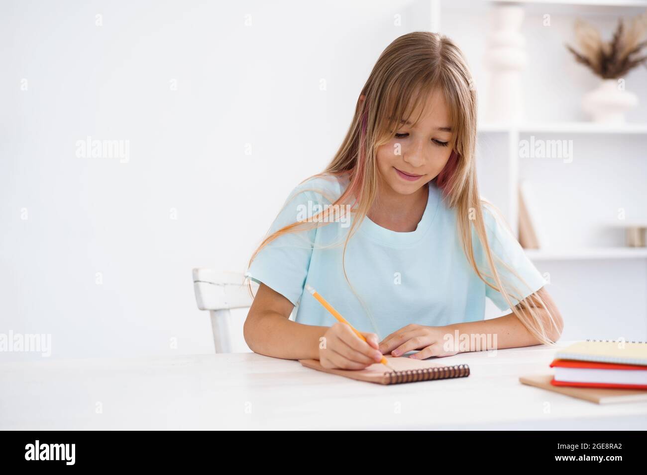 Teenage girl making notes in notepad, doing homework at table at home ...