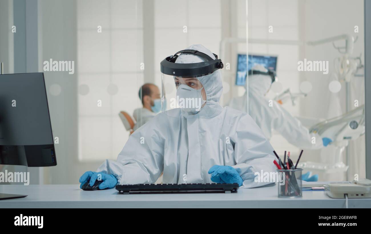 Stomatology assistant sitting at desk using computer while wearing ppe ...