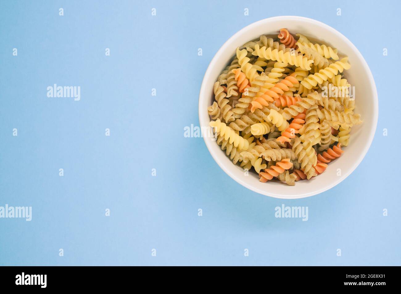 Top view of uncooked tri-color rotini pasta on a bowl isolated on blue ...