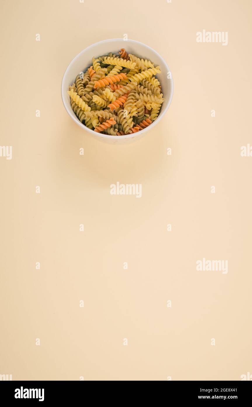 Vertical shot of uncooked tri-color rotini pasta on a bowl isolated on ...