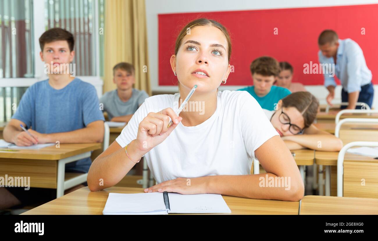 Girl high school student listening to teacher and making notes during ...