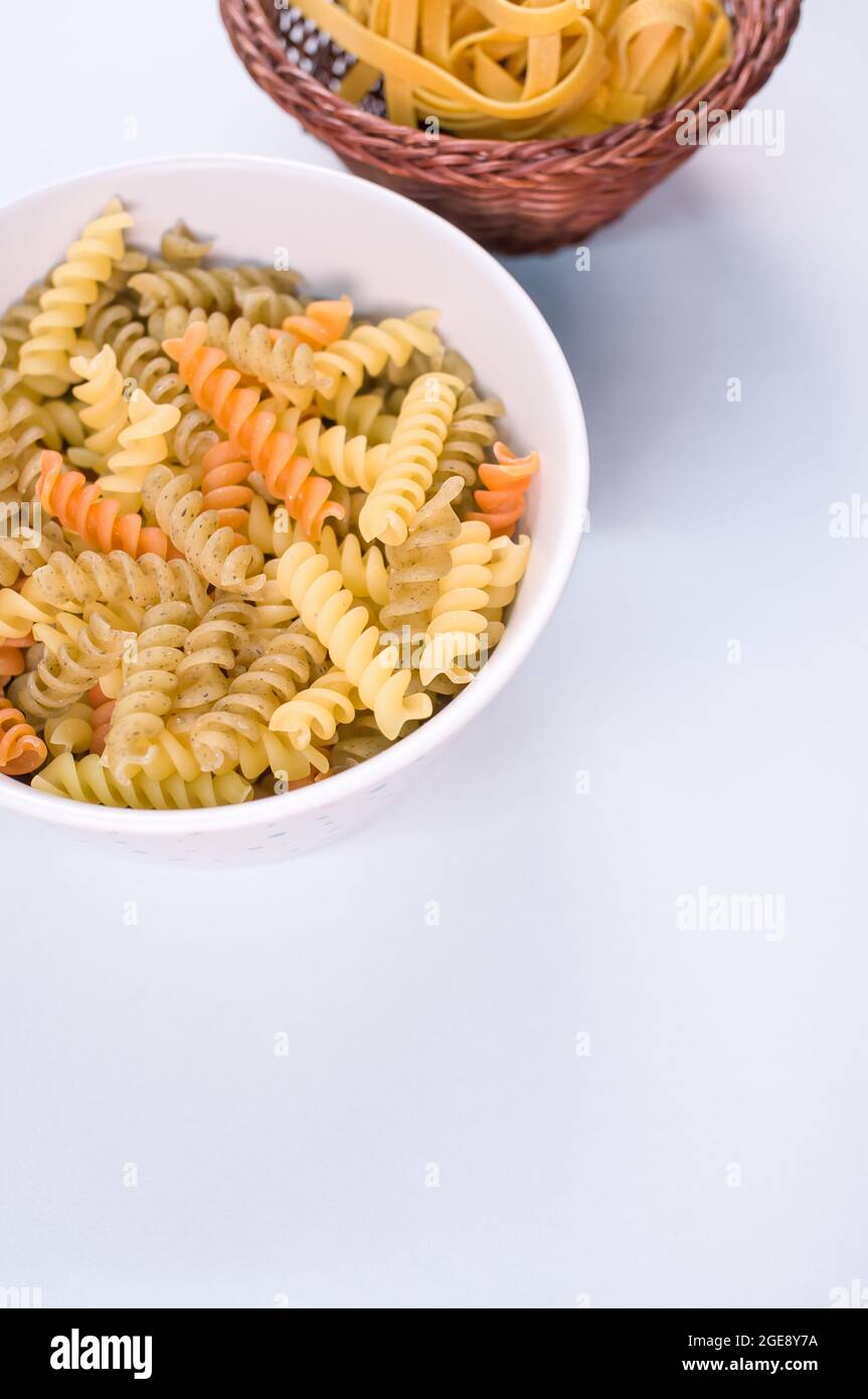 Vertical shot of tri-color rotini and fettuccine pasta on a bowl ...