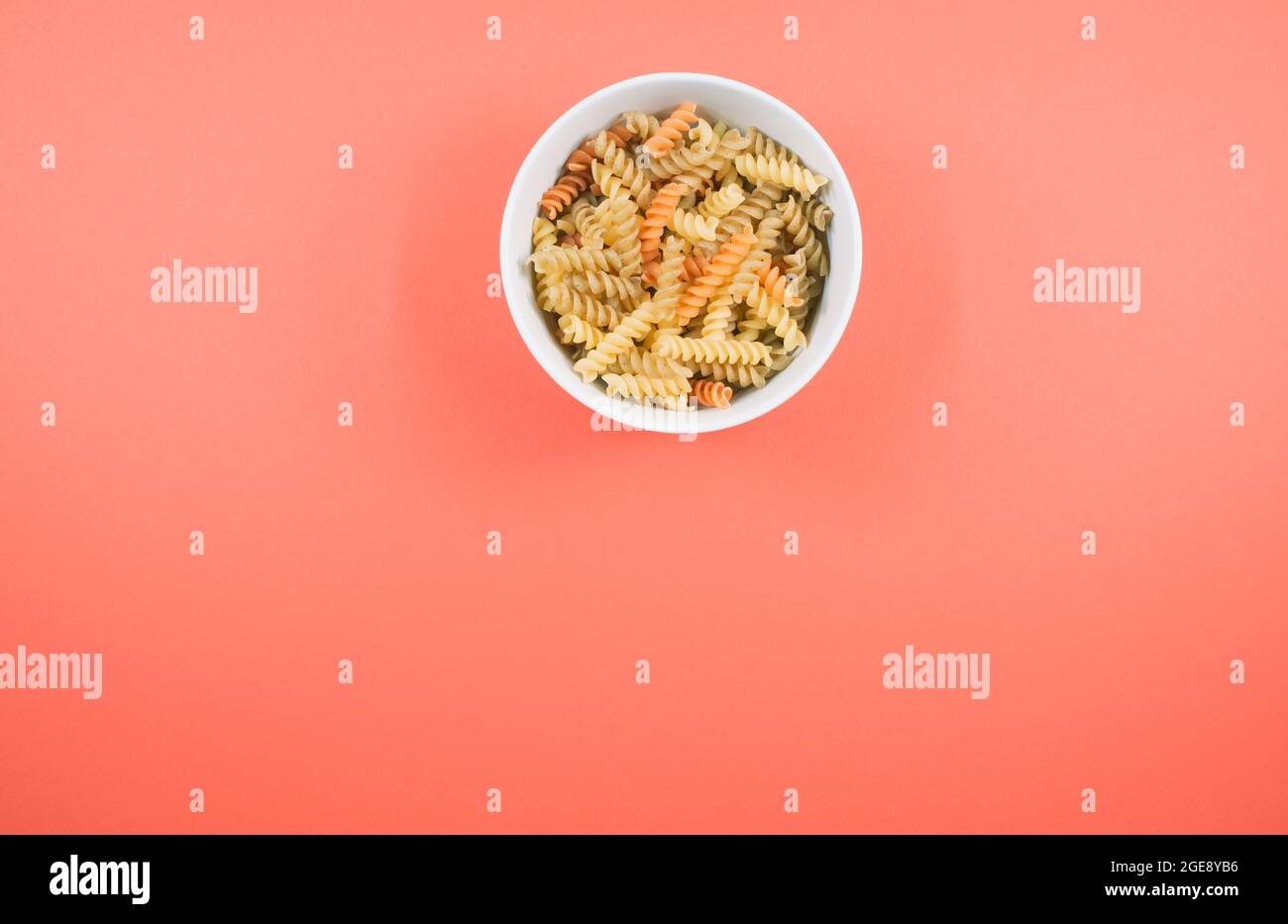 Top view of uncooked tri-color rotini pasta on a bowl isolated on pink ...