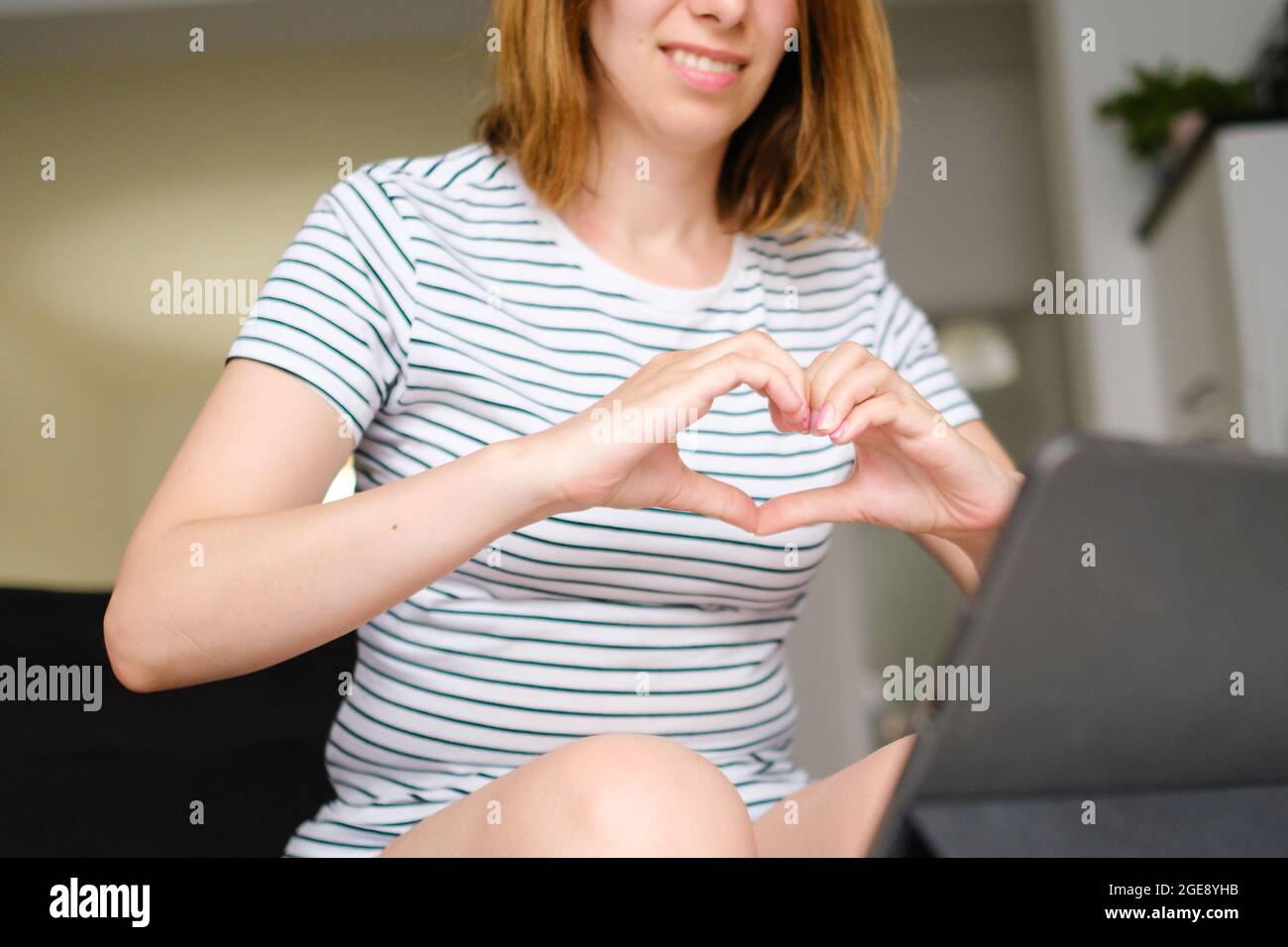 Smiling young woman using laptop for online talking with colleges or friends and shows sign ...