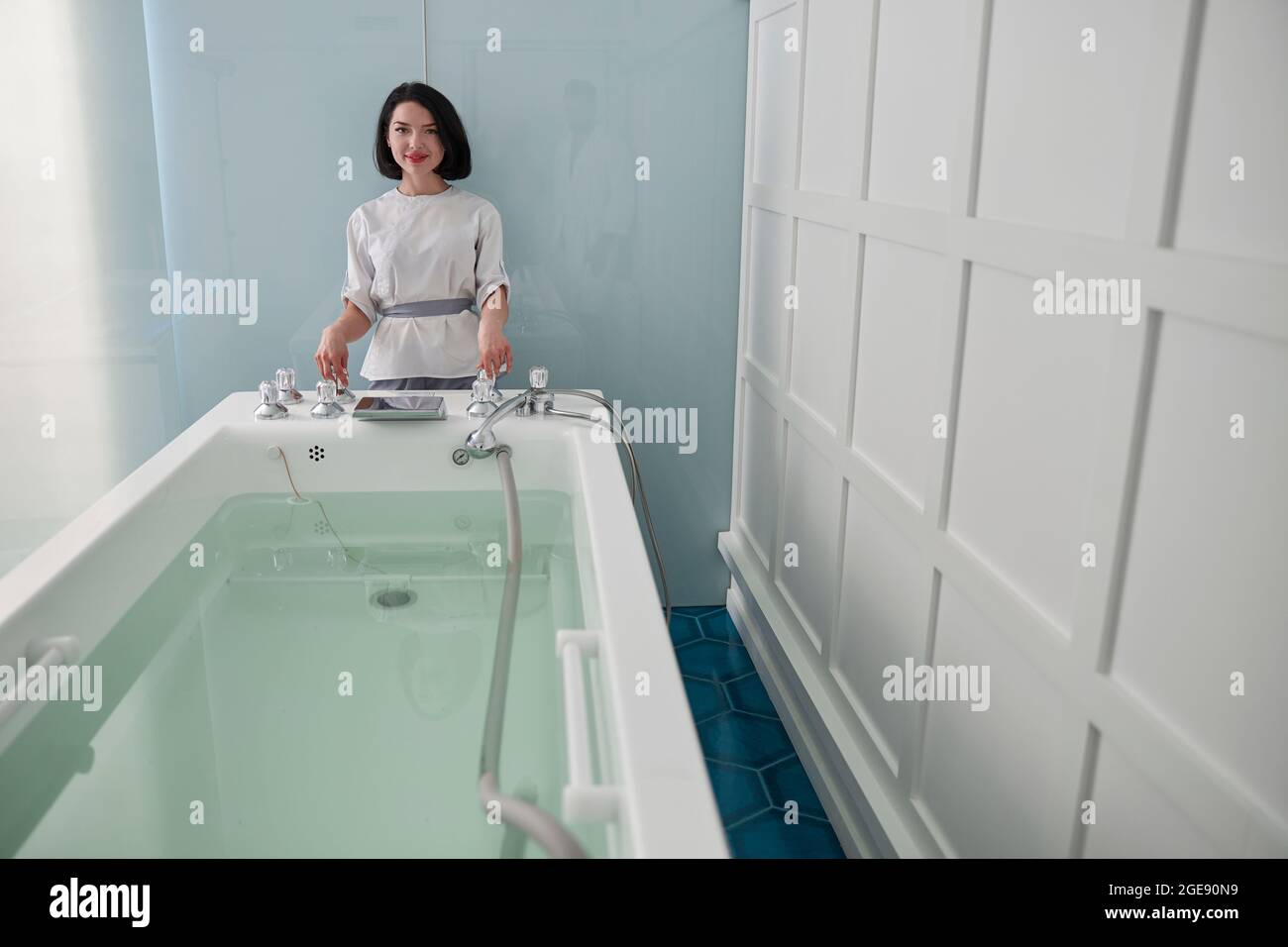 Smiling assistant prepares hydro massage bath full of clear water in ...