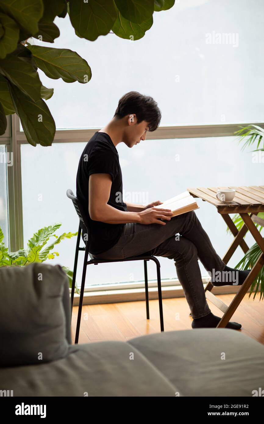 Young Chinese man reading book at home Stock Photo - Alamy