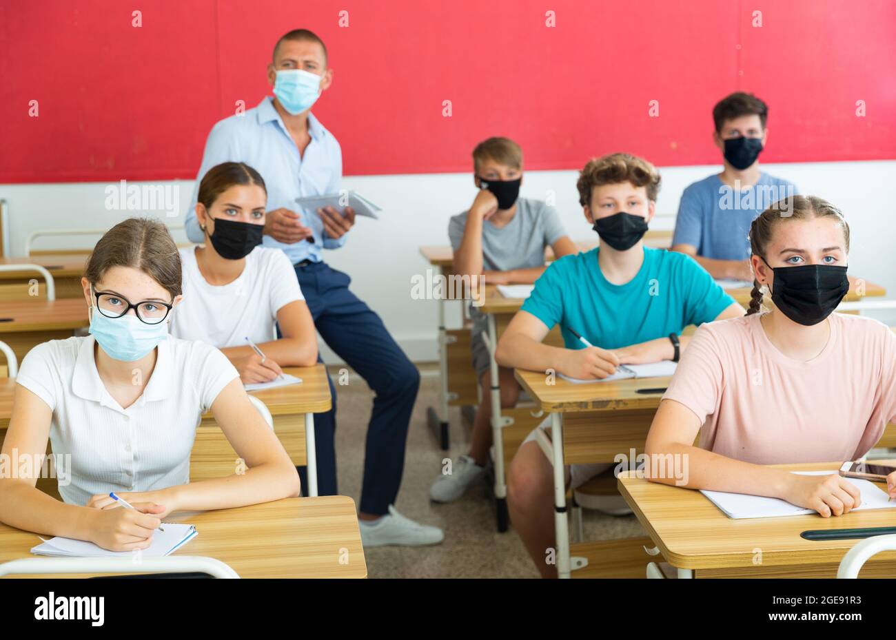 Focused teenage students in protective face masks studying in classroom ...