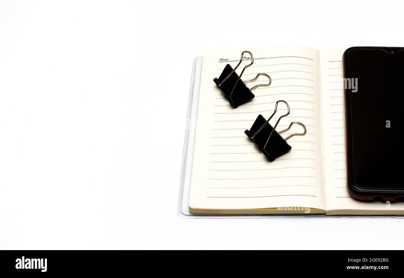 An open diary with a smartphone and black binder clips on white ...