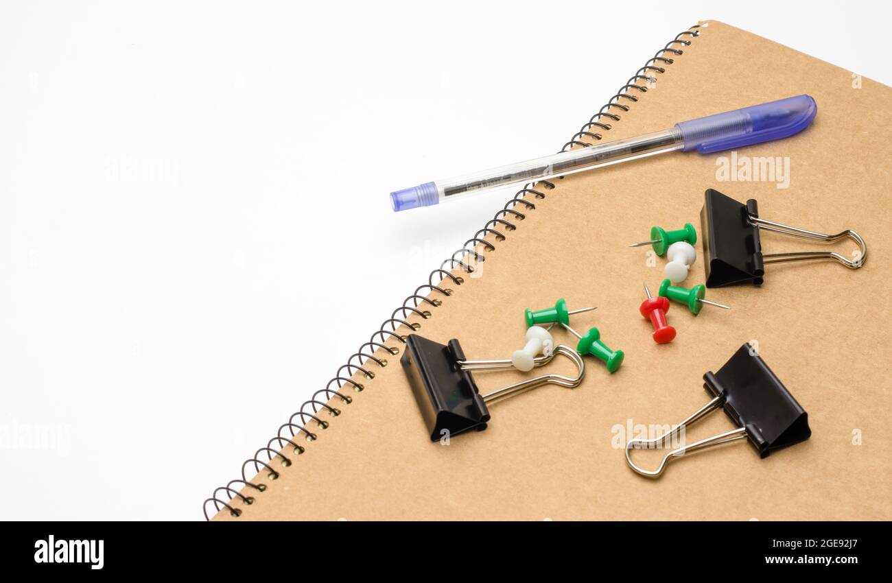 A notepad with a used pen, black binder clips, and pushpins on white ...