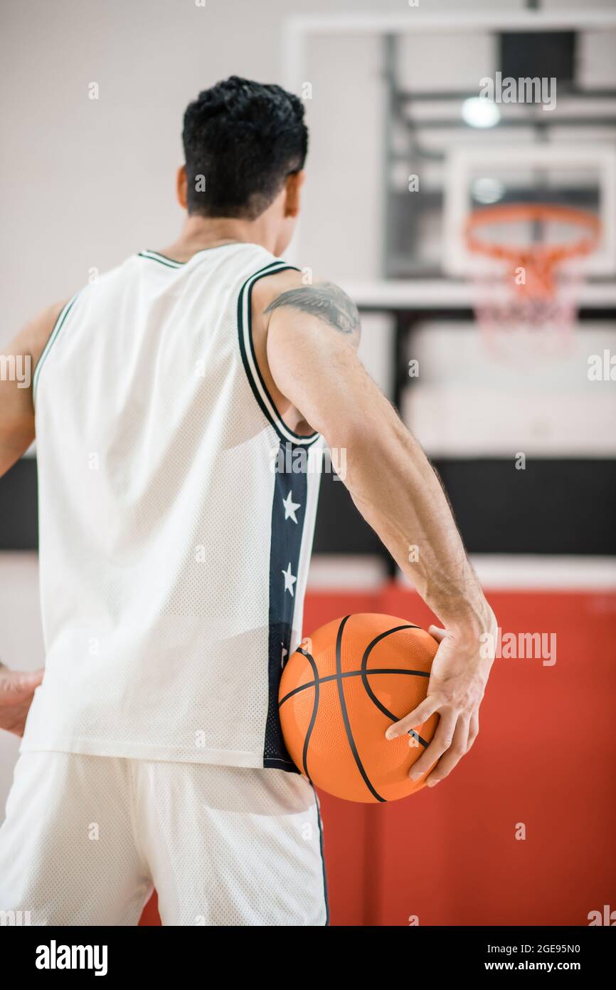 Man in white sportswear holding a big orange ball in hands Stock Photo ...