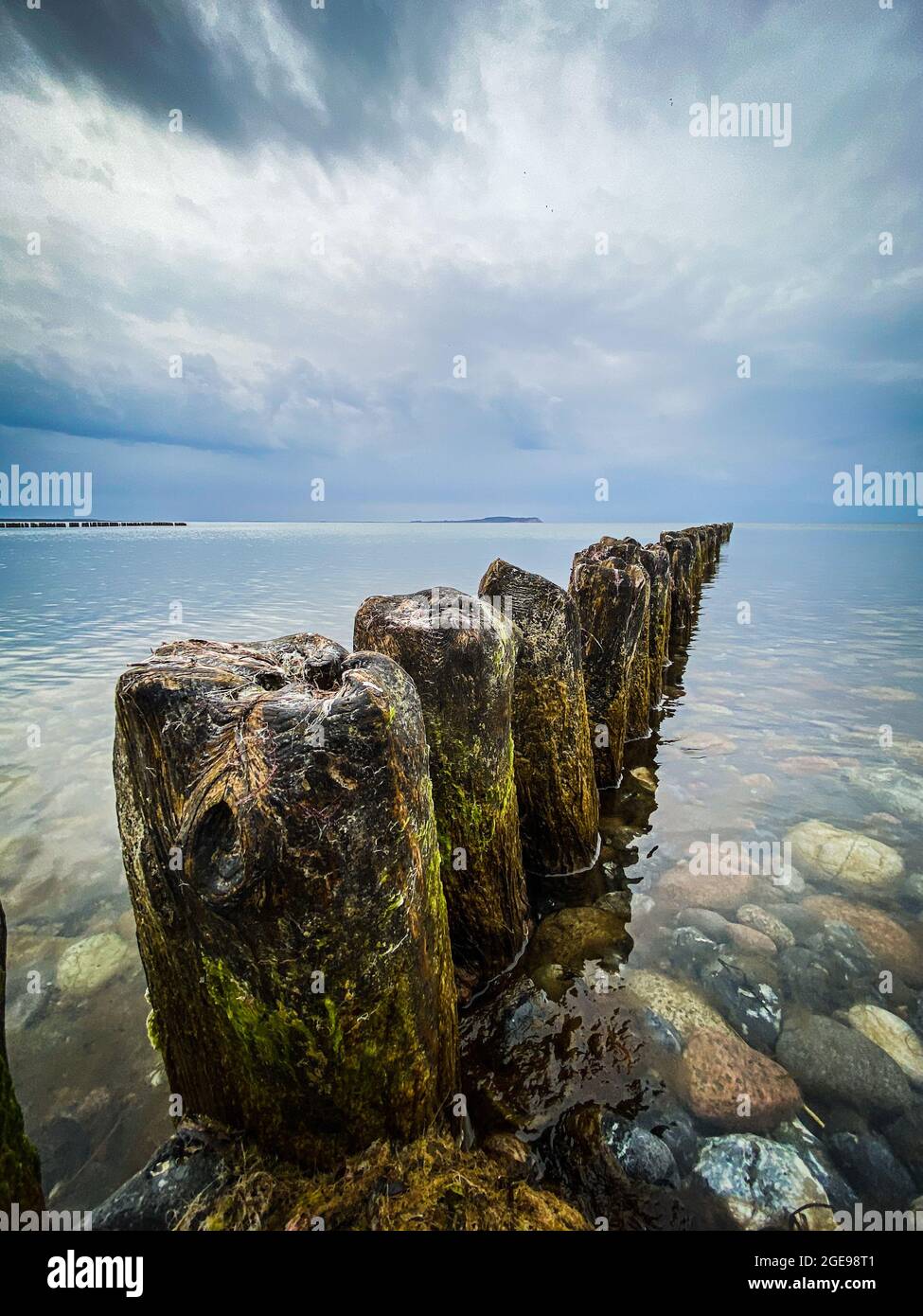 Vertical shot of wooden wave breakers on the coast under a cloudy sky ...