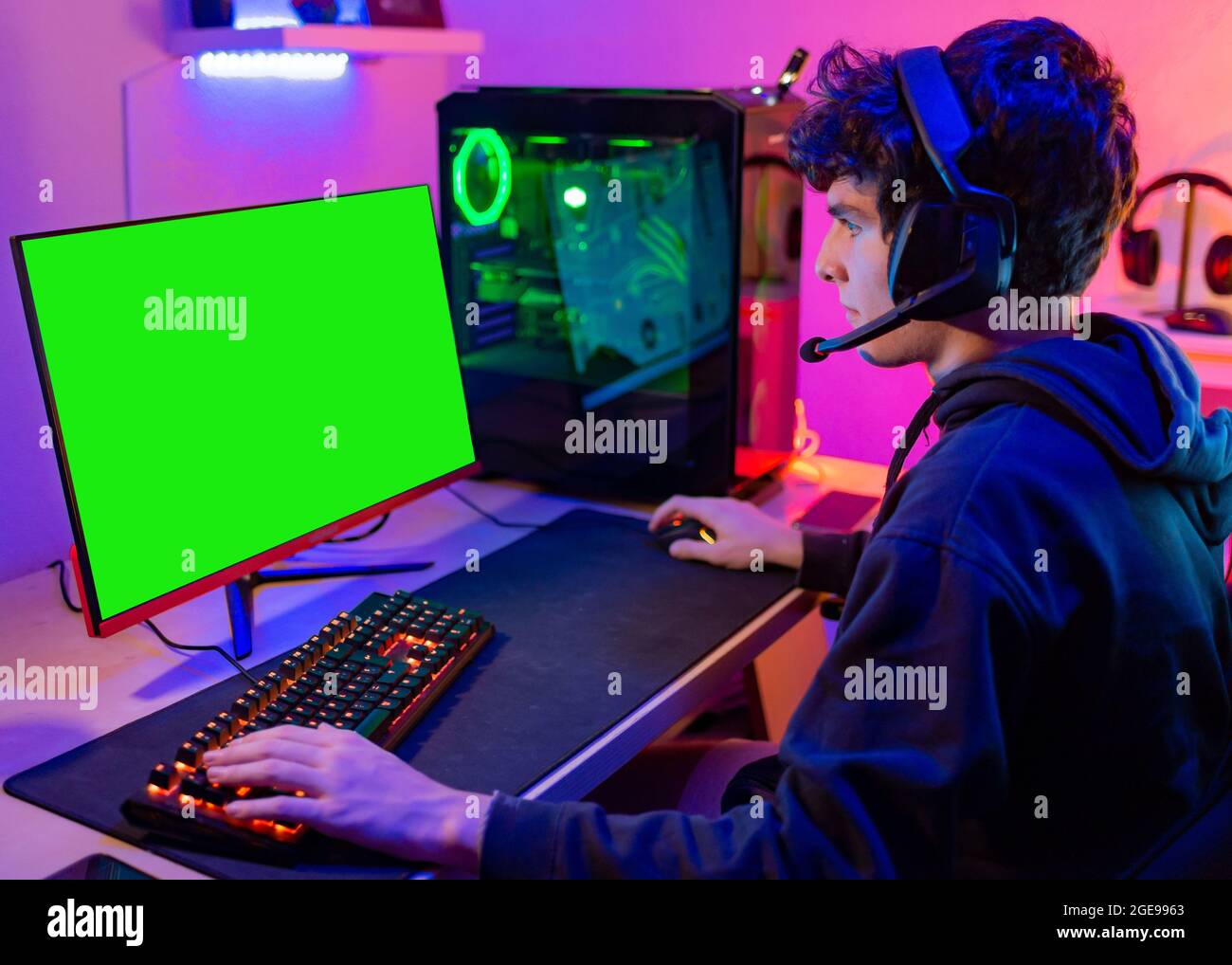 Caucasian young teenager plays computer in his room with colored lights ...