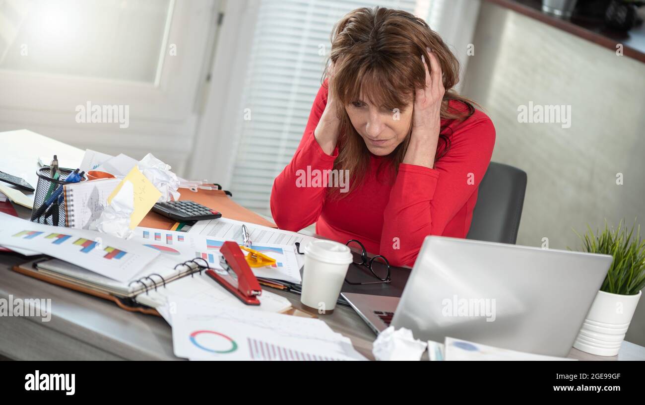 Overworked mature businesswoman sitting at a messy desk Stock Photo - Alamy