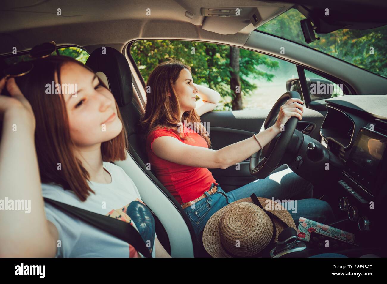 Two young female friends driving in car, enjoy road trip in summer ...