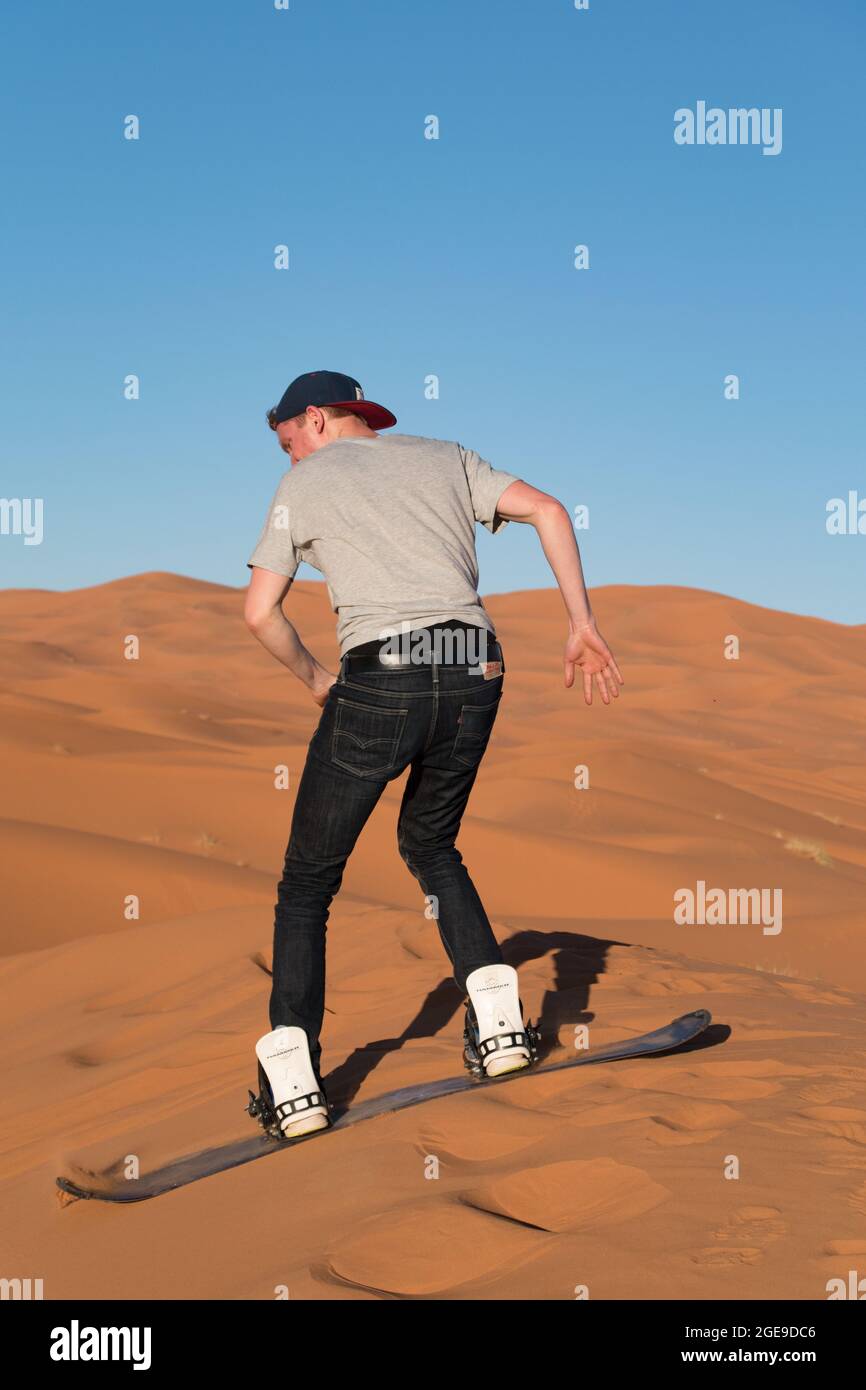 Vertical back view of a young male snowboarding on the sand in the ...