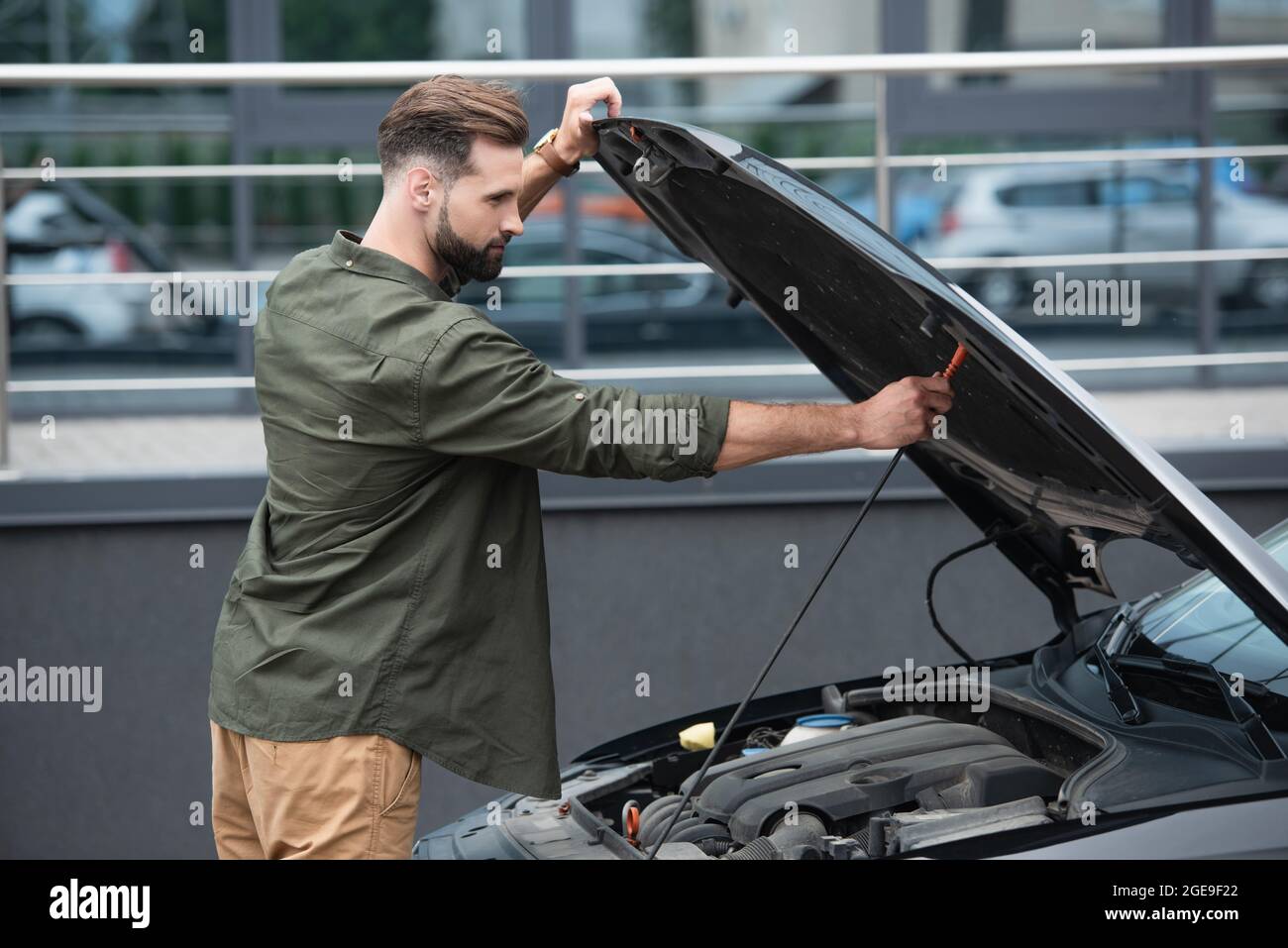 Side view of man opening hood of auto outdoors Stock Photo - Alamy