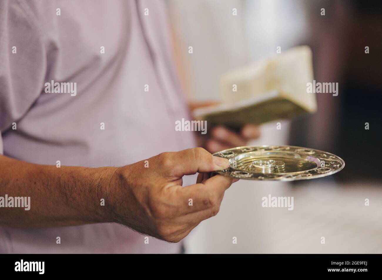 Priest holding plate with stylish wedding rings in church for holy ...