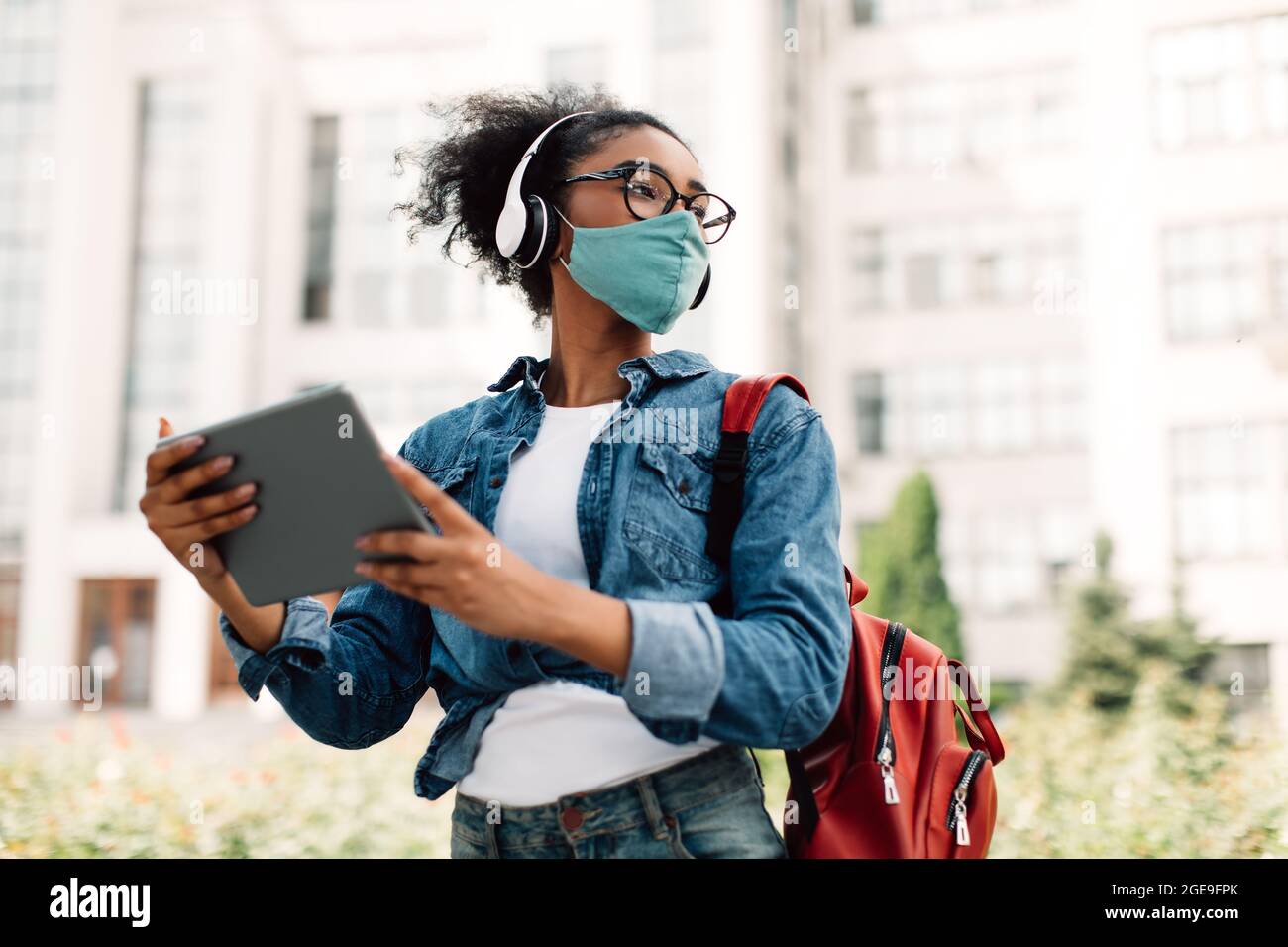 Black Student Girl Using Tablet Wearing Headphones And Mask Outdoors ...