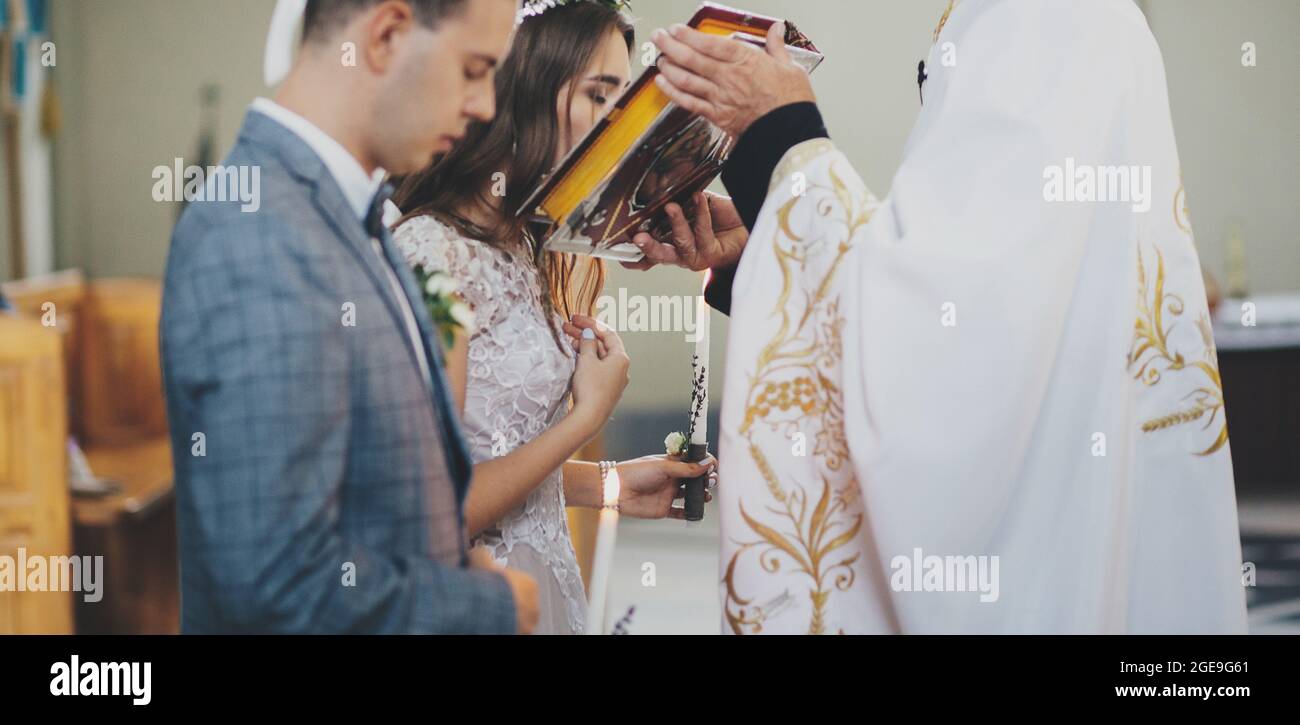 Stylish bride and groom kissing holy bible from priest hands during ...