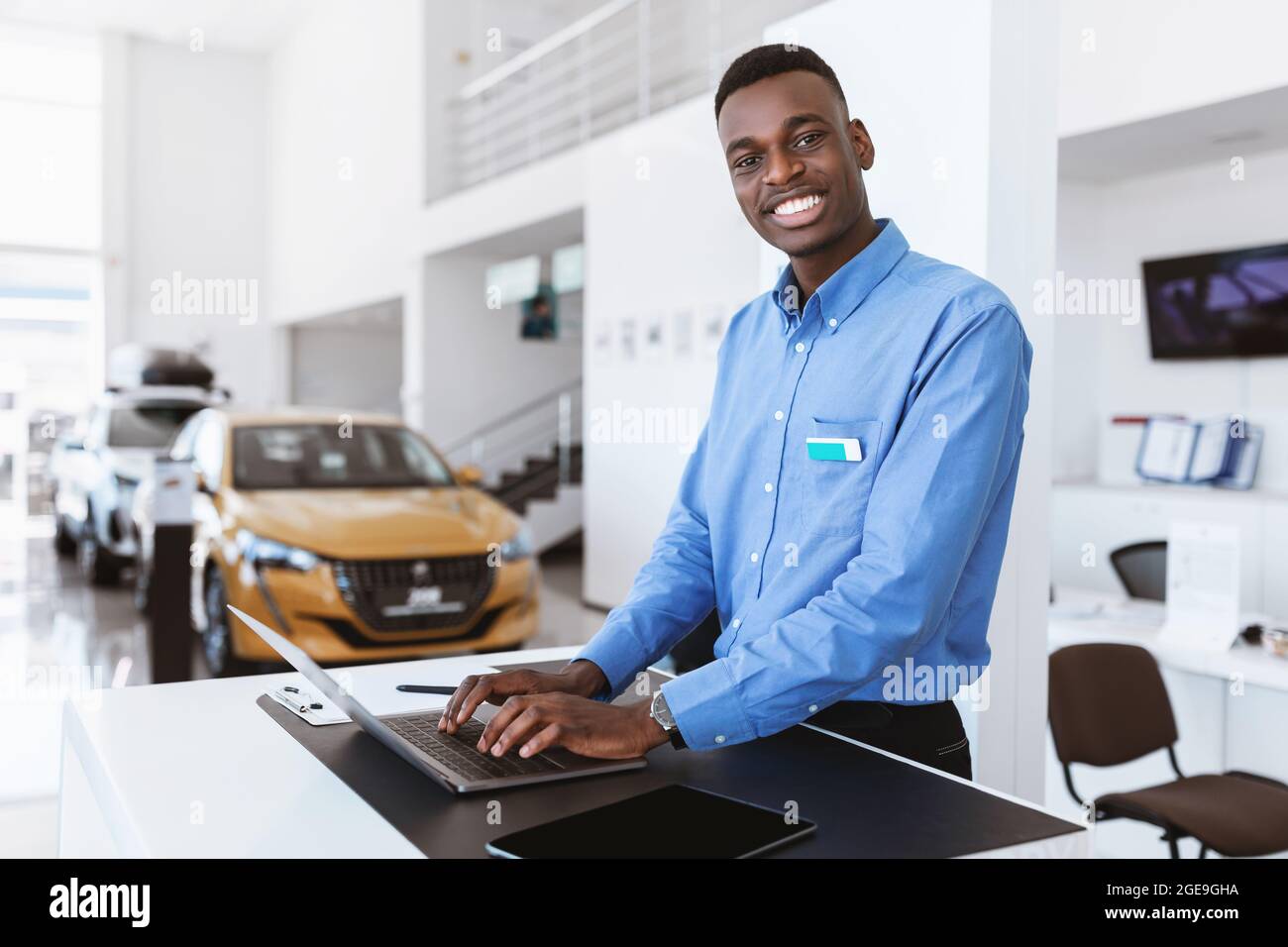 Cheerful black car salesman posing at work desk, smiling at camera ...