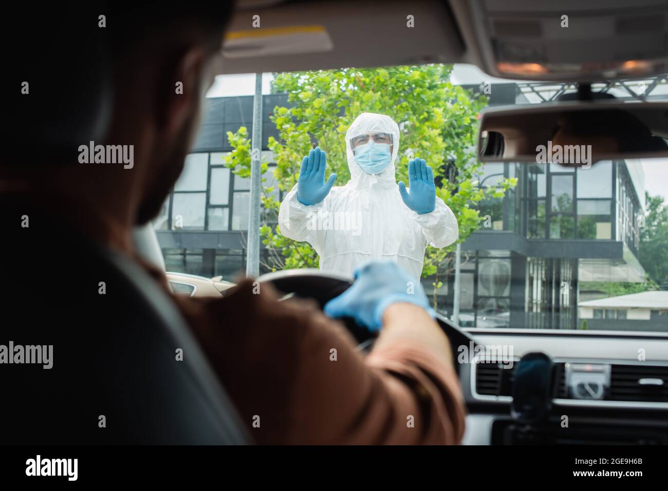 Medical worker in protective suit showing stop at blurred driver in ...