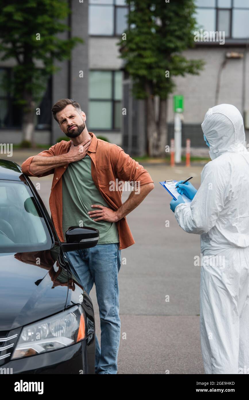 Sick driver standing near car and medical worker writing on clipboard ...