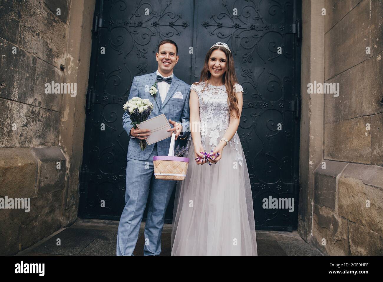 Stylish happy bride and groom throwing candy on background of church ...