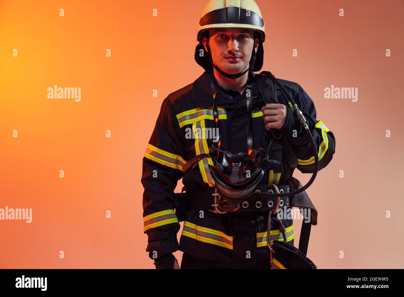 One male firefighter dressed in uniform posing over orange background ...