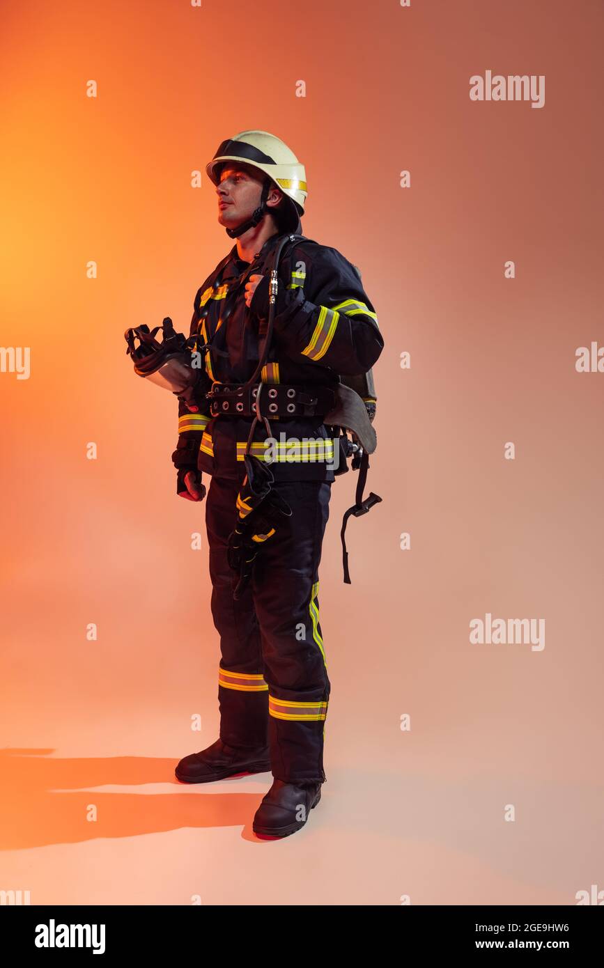 One male firefighter dressed in uniform posing over orange background ...