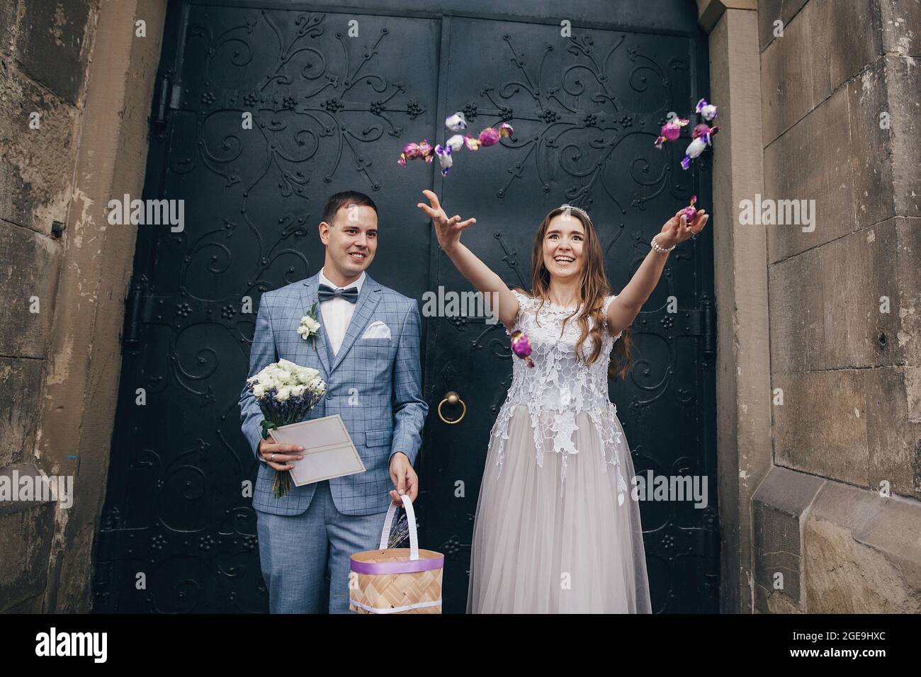 Stylish happy bride and groom throwing candy on background of church ...