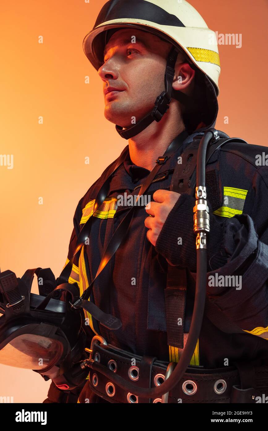 One male firefighter dressed in uniform posing over orange background ...