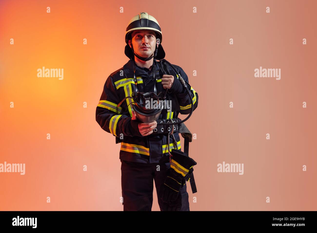 One male firefighter dressed in uniform posing over orange background ...